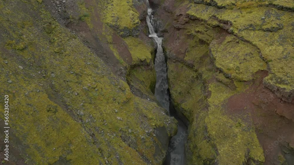 A layered rock gorge with water running down a narrow valley between a ...
