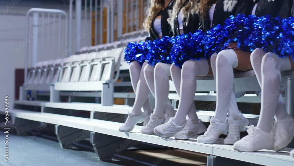 Close up side view of cheerleaders sitting in a row on a bench and ...