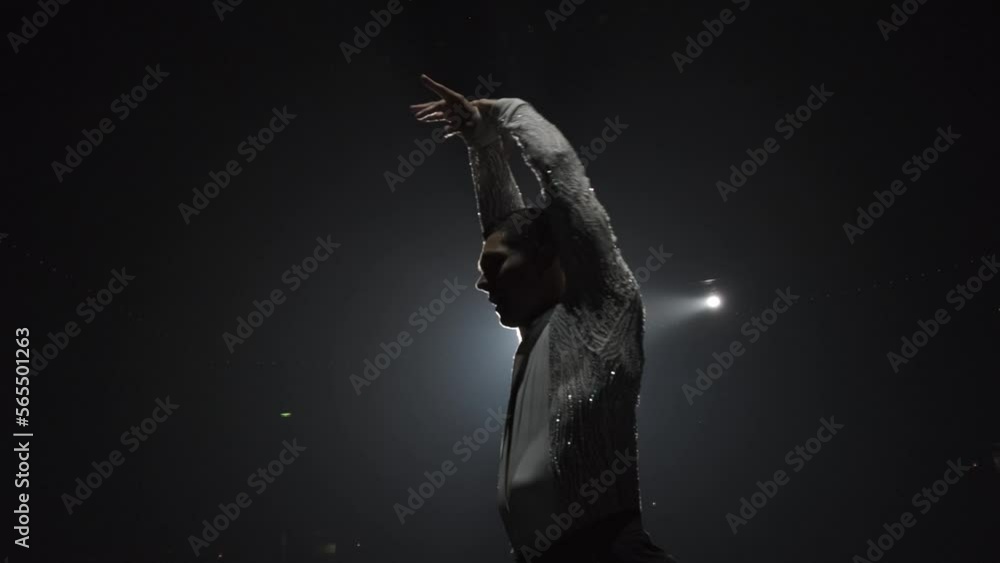 Young dance man in white sparkling shirt in spotlight makes two turns ...