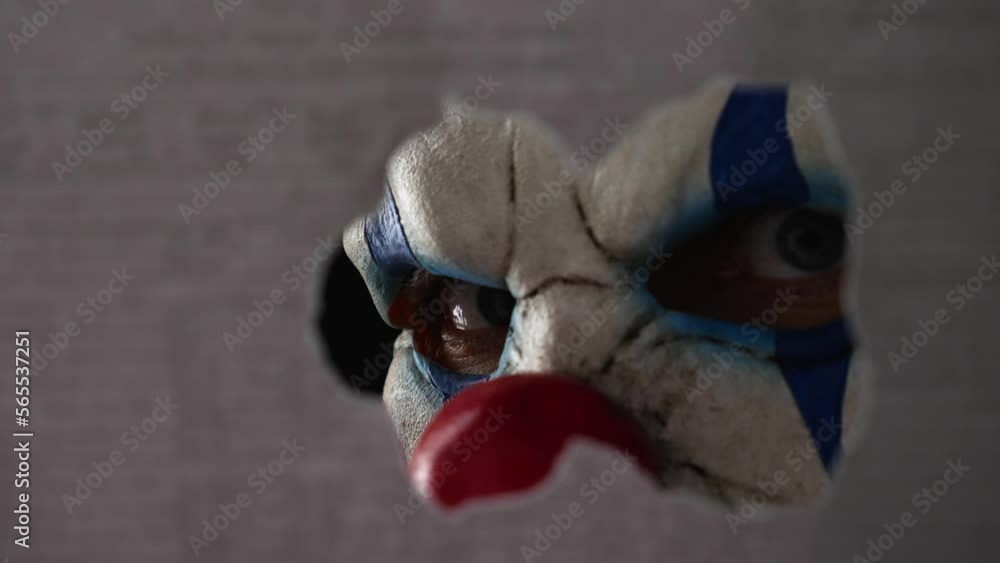 A scary clown face peeking through a hole in the partition. Close-up ...