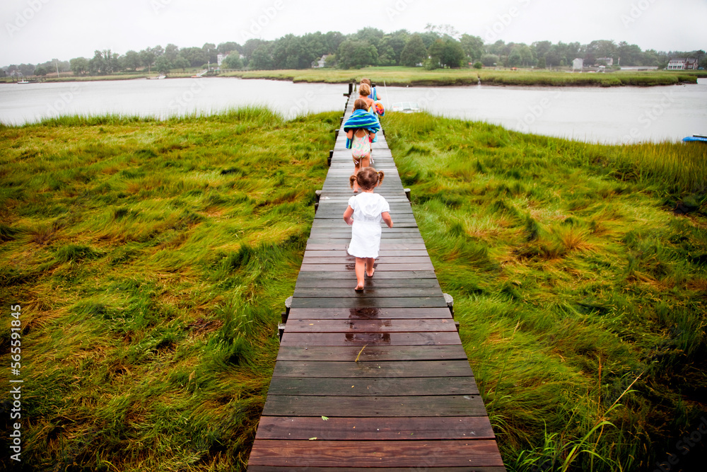 Four young children walk on a raised boardwalk over lush marsh grasses ...