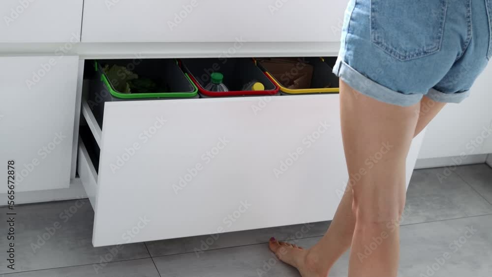 A young woman sorts garbage in containers in the kitchen. Modern ...