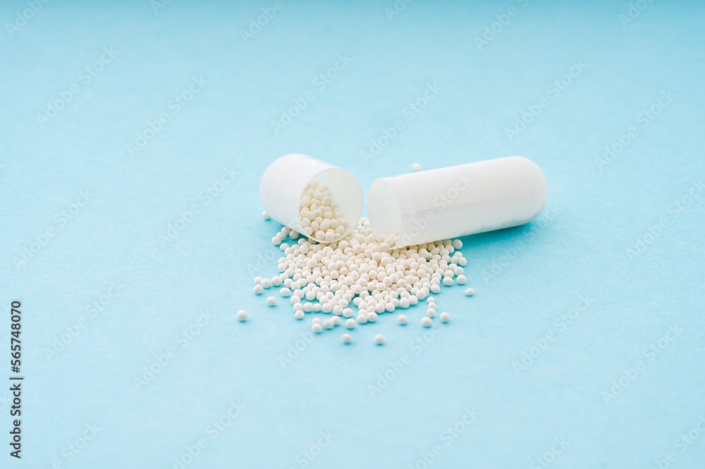 Gel capsule opened. White medicine powder spilled out on light blue ...