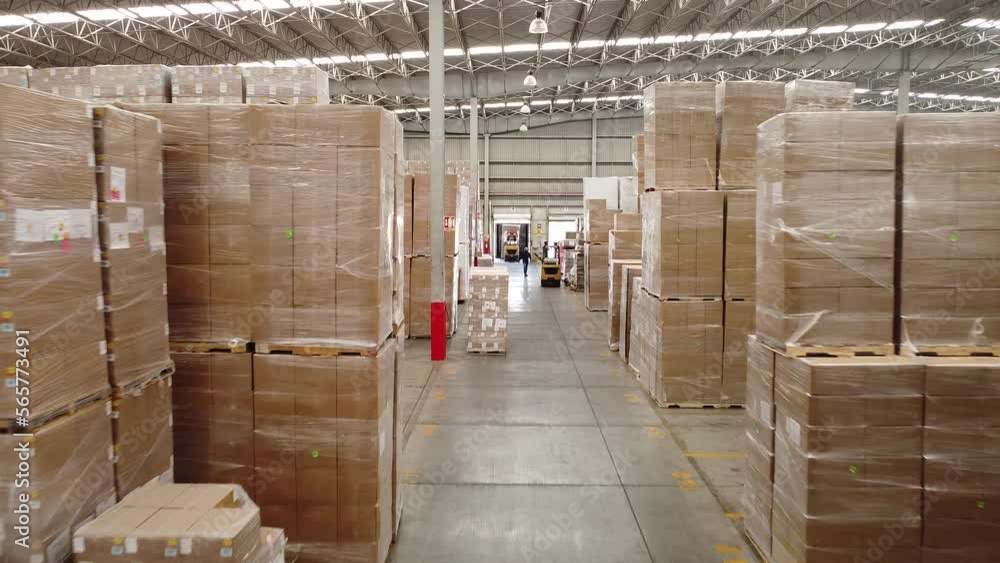Vuelo de drone en interior de un almacén con cajas apiladas, pallets, productos empaquetado y ...