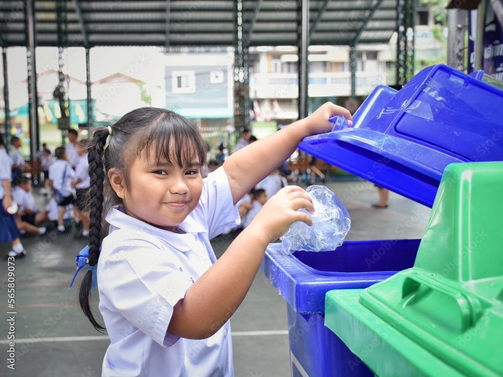 Elementary school students are throwing garbage into the bin with a ...