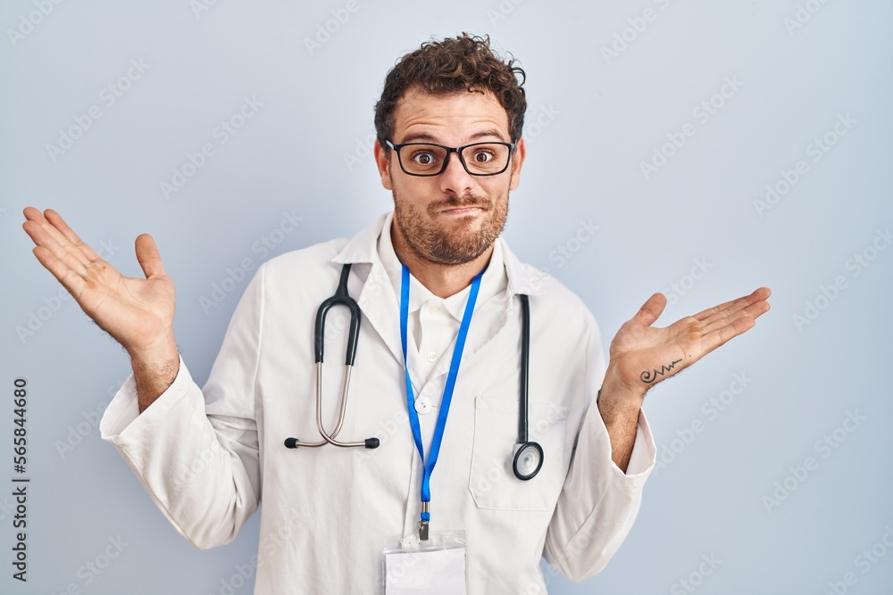 Young hispanic man wearing doctor uniform and stethoscope clueless and ...