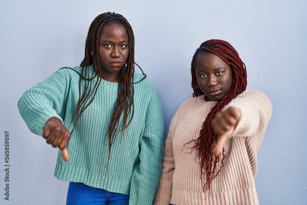 Two african woman standing over blue background looking unhappy and ...