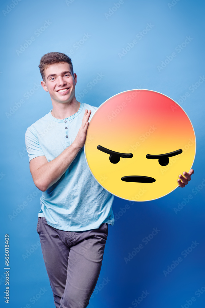 Social network concept. Happy young man holding yellow angry emoji face ...