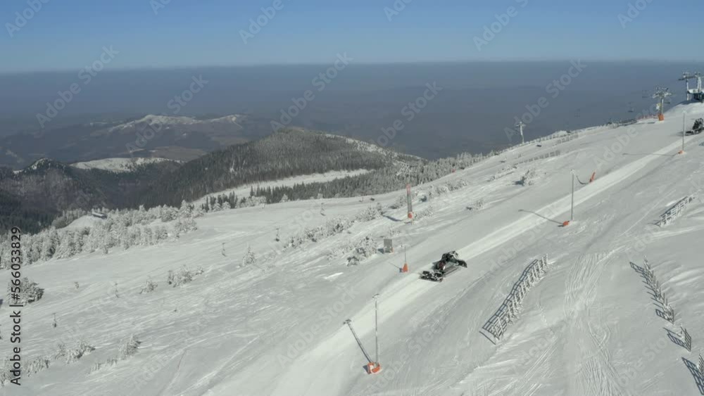 4K aerial view of a snowcat tractor at a ski resort clearing snow ...