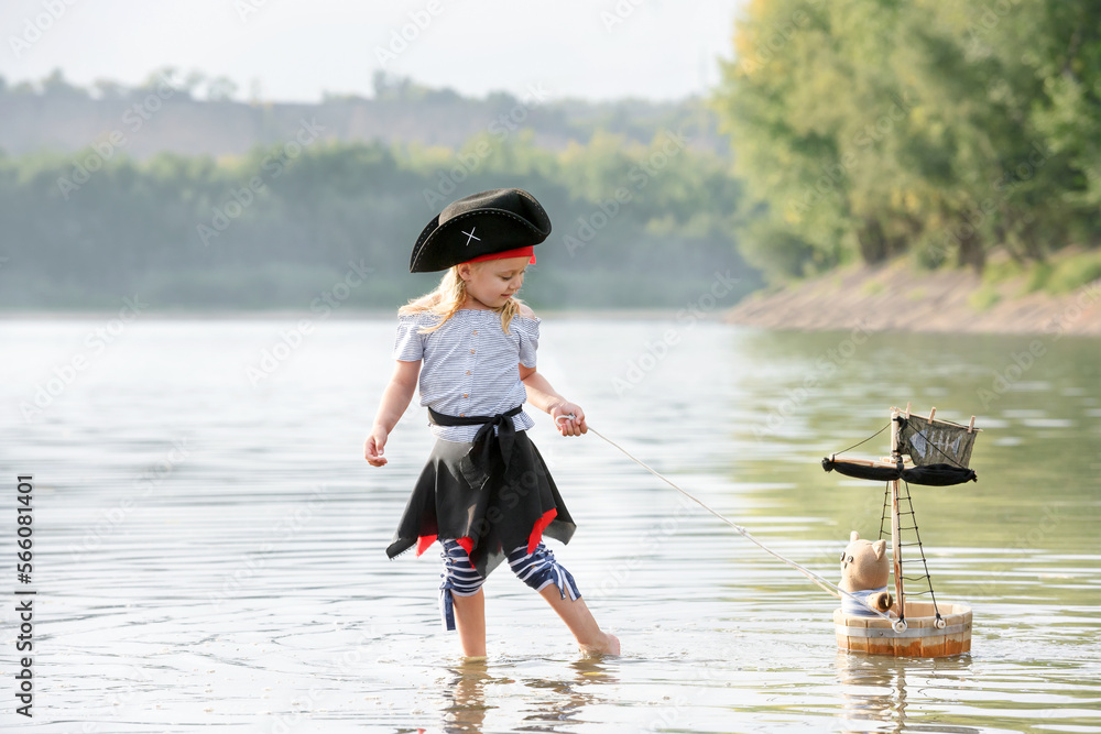 Children in pirate costumes play on a wooden raft at sunset. Two girls ...