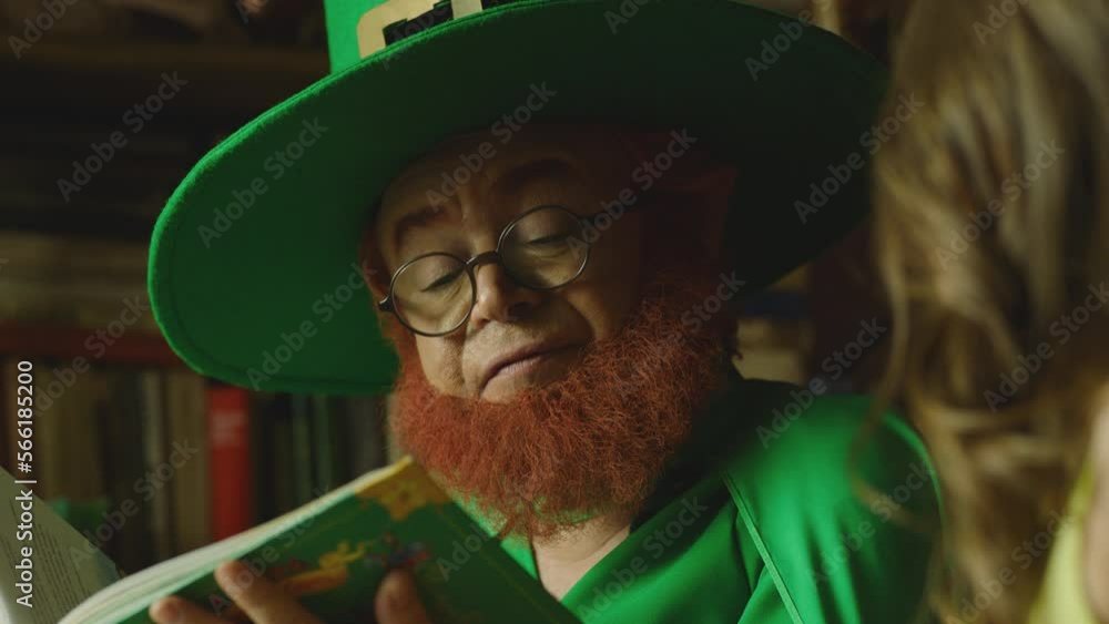 Old leprechaun is reading book , telling fairy tale story for little ...