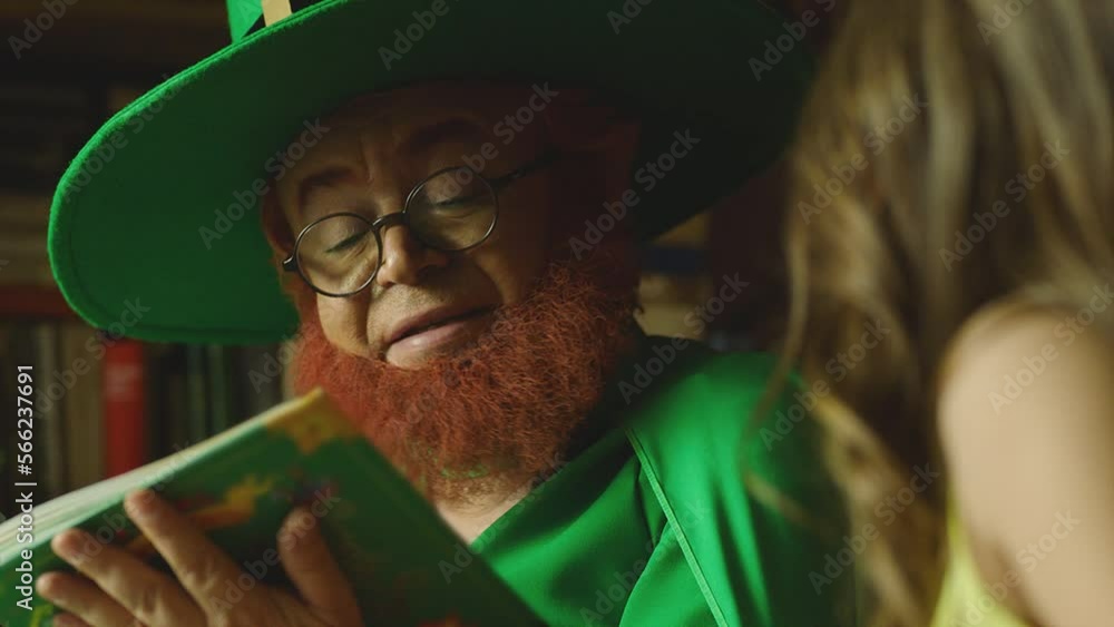 Old leprechaun is reading book , telling fairy tale story for little ...