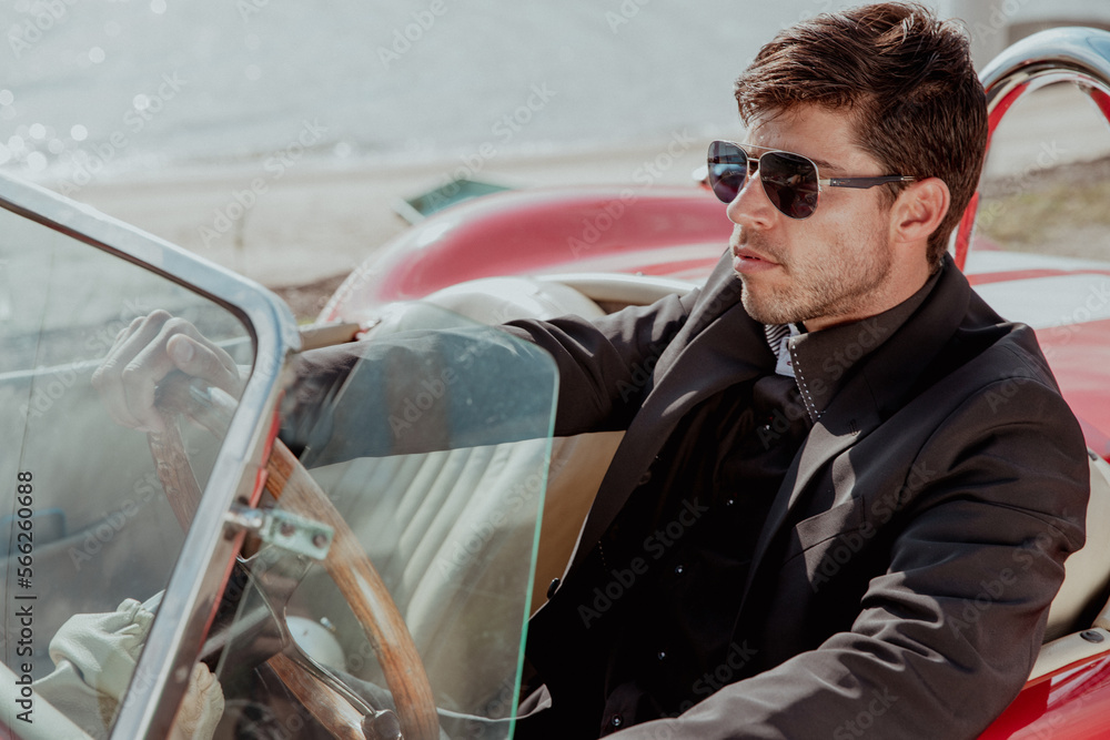 young man in convertible car looking at camera, smiling, man wears suit ...