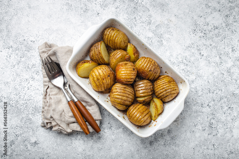 Hasselback potatoes with herbs in white ceramic casserole dish on white ...