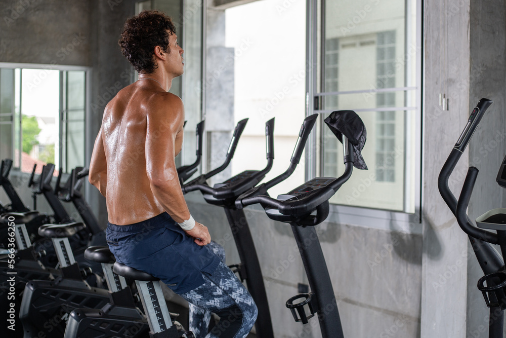 Caucasian topless athletic man cardio riding on bicycle at gym fitness ...