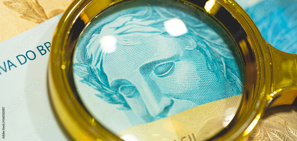 Notas do Real Brasileiro sobre uma mesa com uma lupa dourada na ...