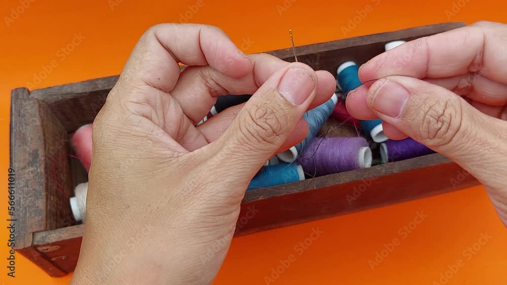 Footage of a human hand threading a needle with a white background and ...