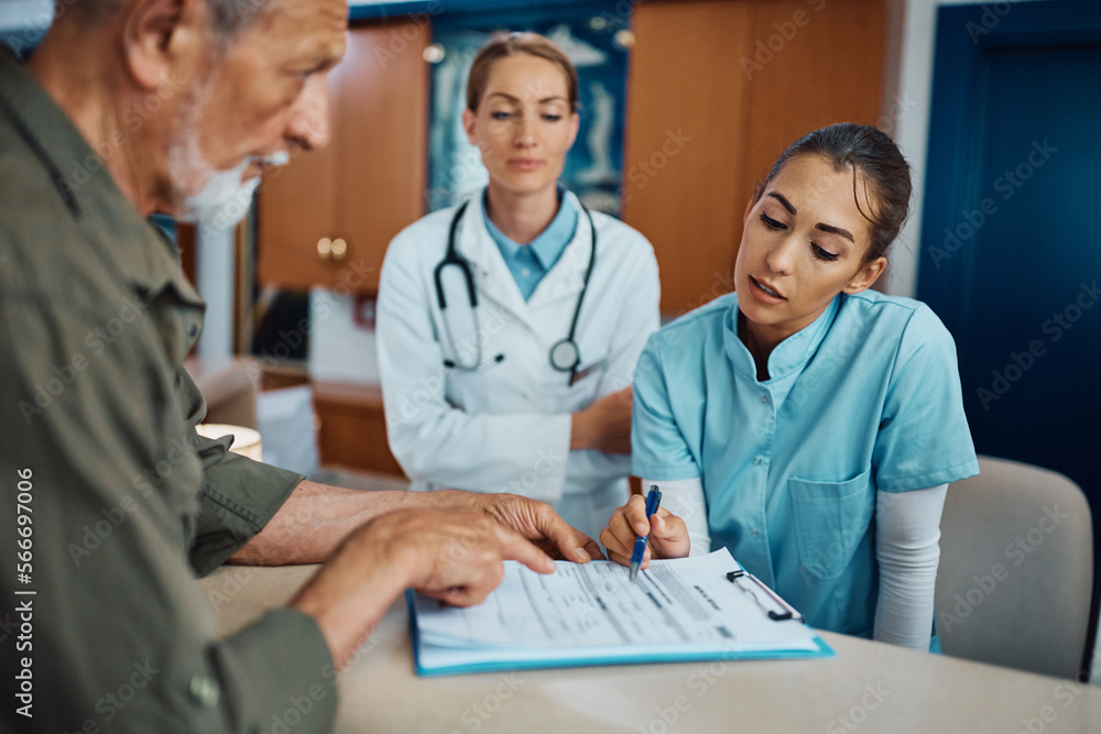 Young nurse assisting senior man to fill out medical documents at ...
