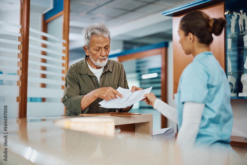 Senior man giving to nurse his medical paperwork while checking in at ...
