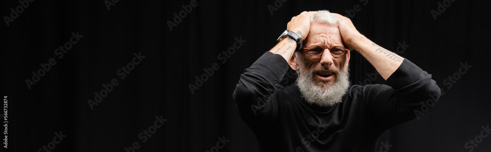 frustrated tattooed actor holding hands on head while playing dramatic ...