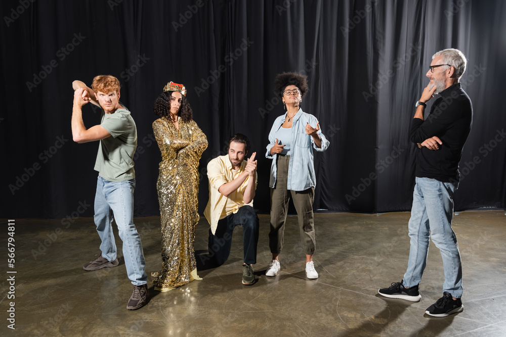 grey haired art director looking at multiracial woman in queen costume ...