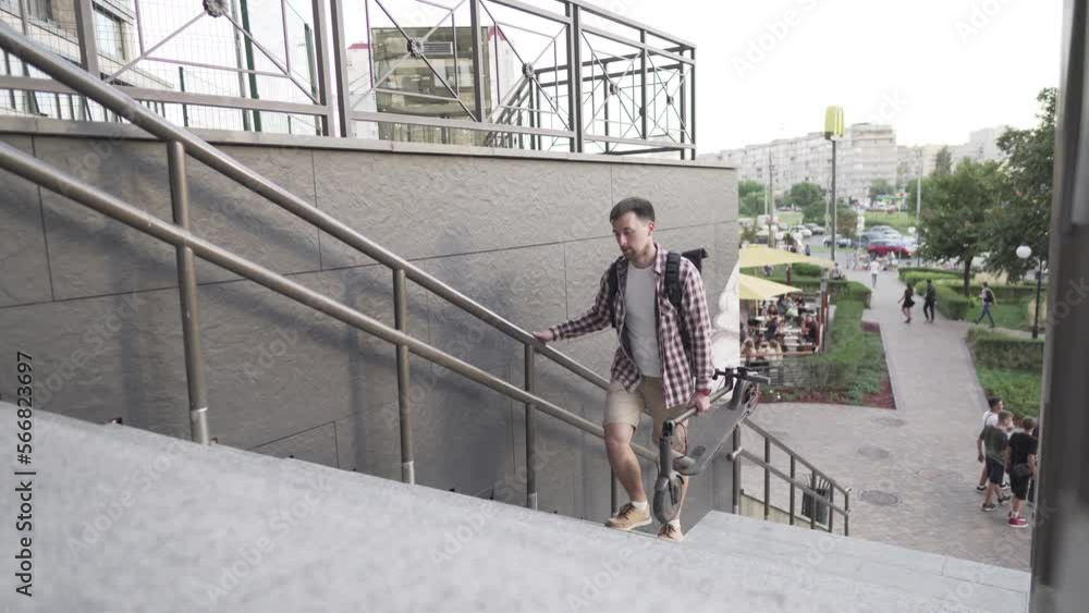 Man walking with folded electric scooter up stairs incity near modern ...