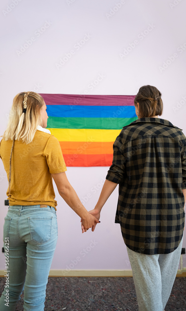 Two proud lesbian women holding hands, gazing at the LGBT symbol of ...