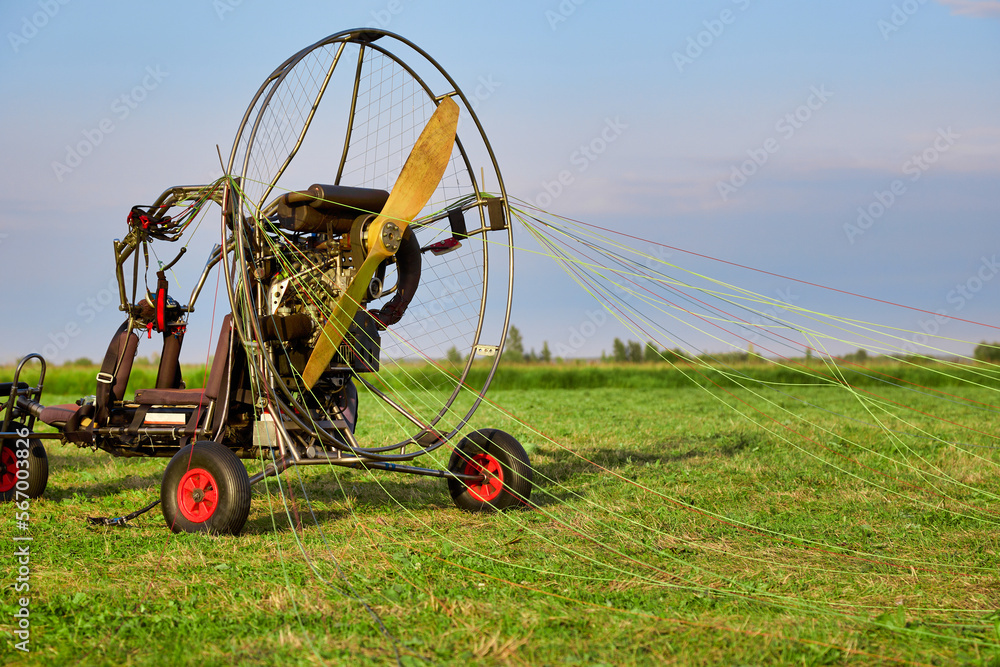 Modern motorized paraglider on a green launch pad in a field is ready ...