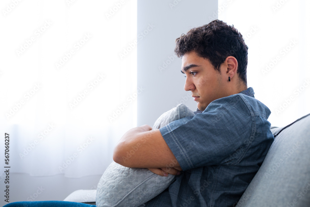 Sad hispanic boy hugging pillow. Pensive teenager suffering depression ...