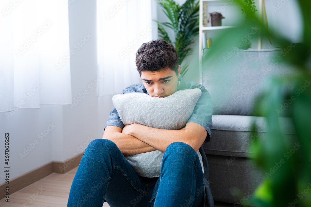 Sad hispanic teenager boy sitting on floor and hugging pillow ...