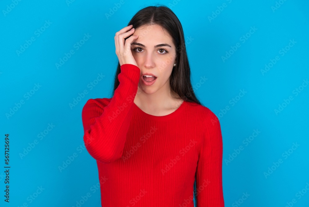 Embarrassed young brunette girl wearing red T-shirt against blue wall ...