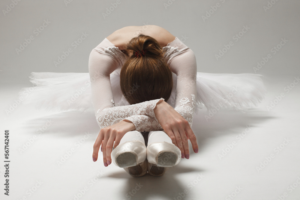 beautiful ballerina in white ballet clothing sitting on floor bent over ...