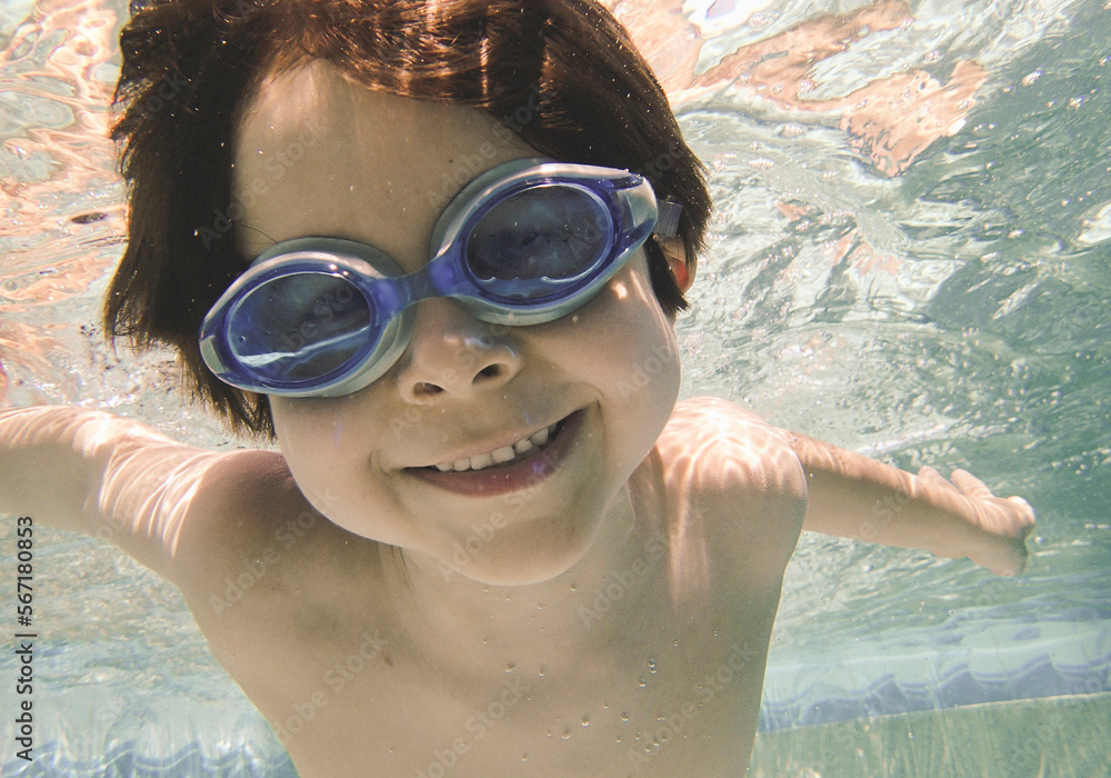 Portrait of shirtless smiling boy swimming underwater in swimming pool ...