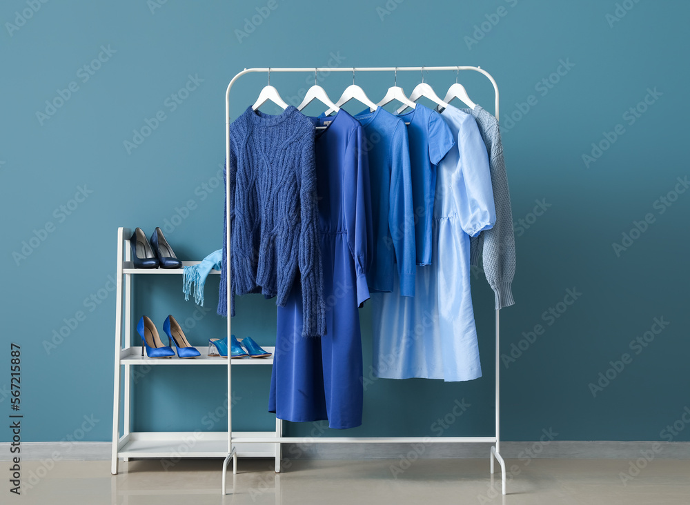 Rack with blue clothes and shoe stand near color wall Stock Photo ...