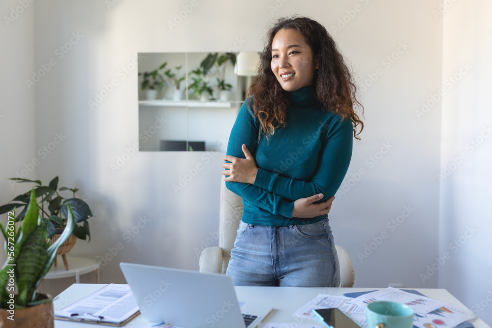 Smiling young Asian female employee stand at desk in office look in ...