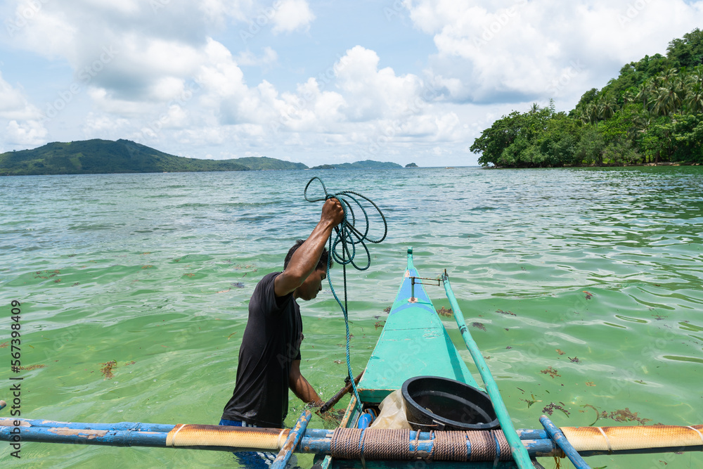 young Filipino fisherman picking up the anchor to go fishing ...