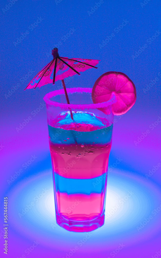 bright rich neon cocktail in a tall glass with an umbrella and a piece ...