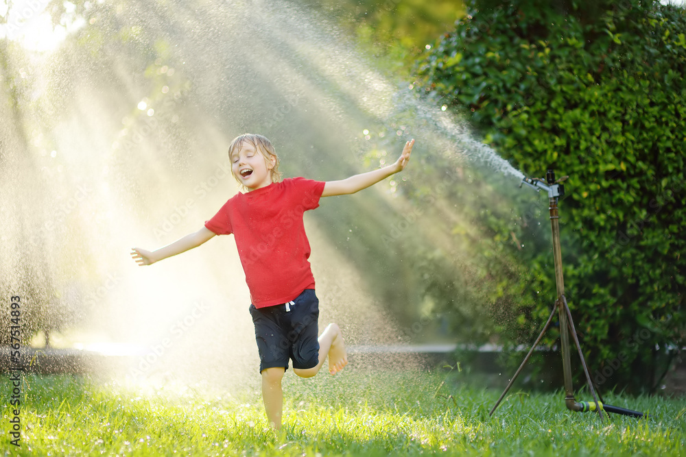 Funny little boy playing with garden sprinkler in sunny backyard ...