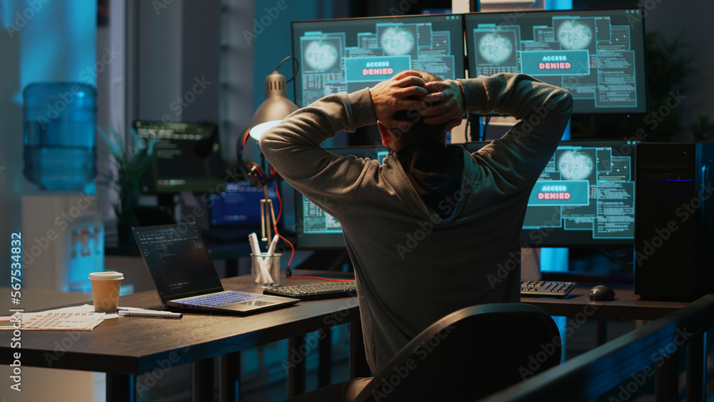 Frustrated hacker using computer to break into corporate data servers, working under pressure ...