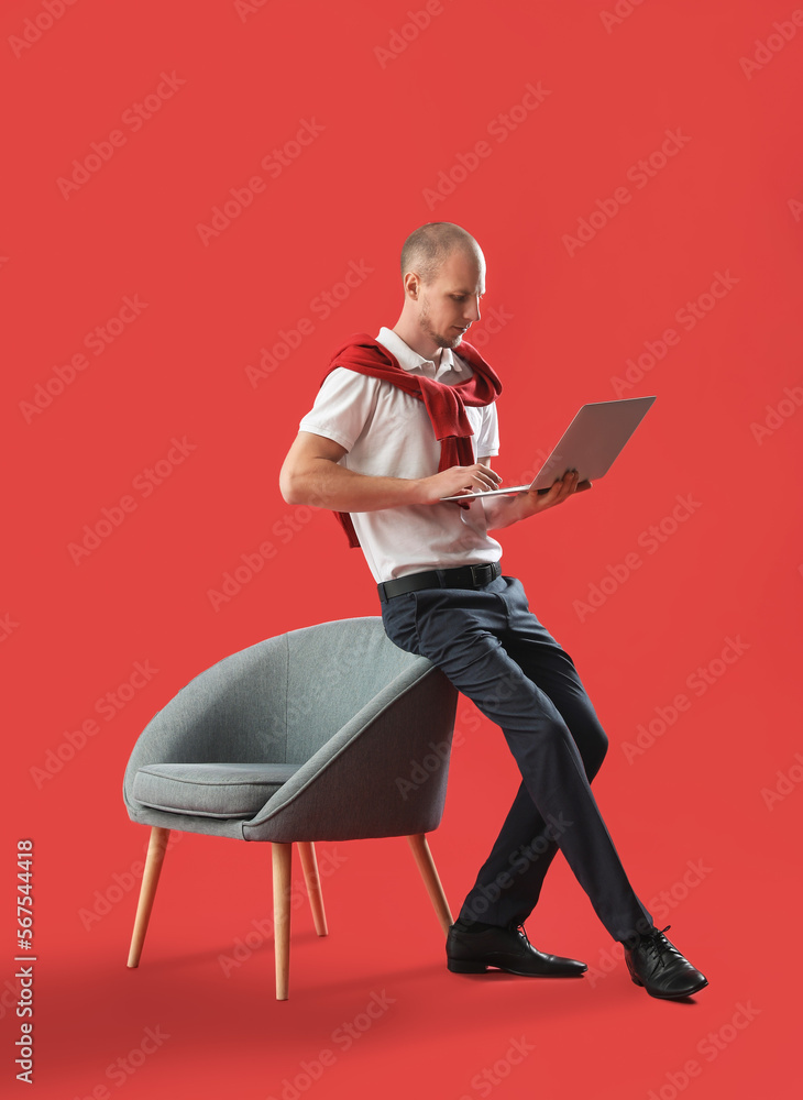 Handsome man using laptop beside soft armchair on red background Stock ...