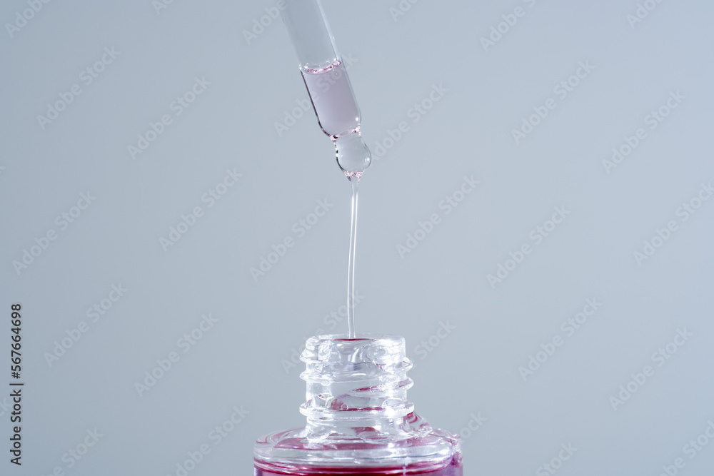 Pink face oil drop from glass pipette dropper. Macro close up for ...