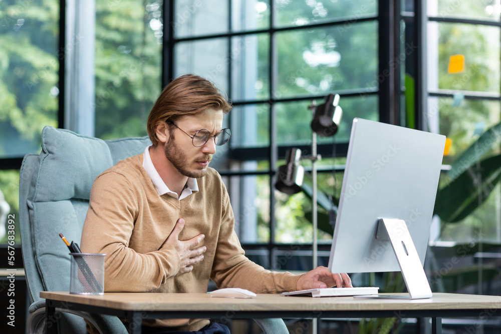 Heart attack at work. Panic attack. A young man is sitting at a desk in ...
