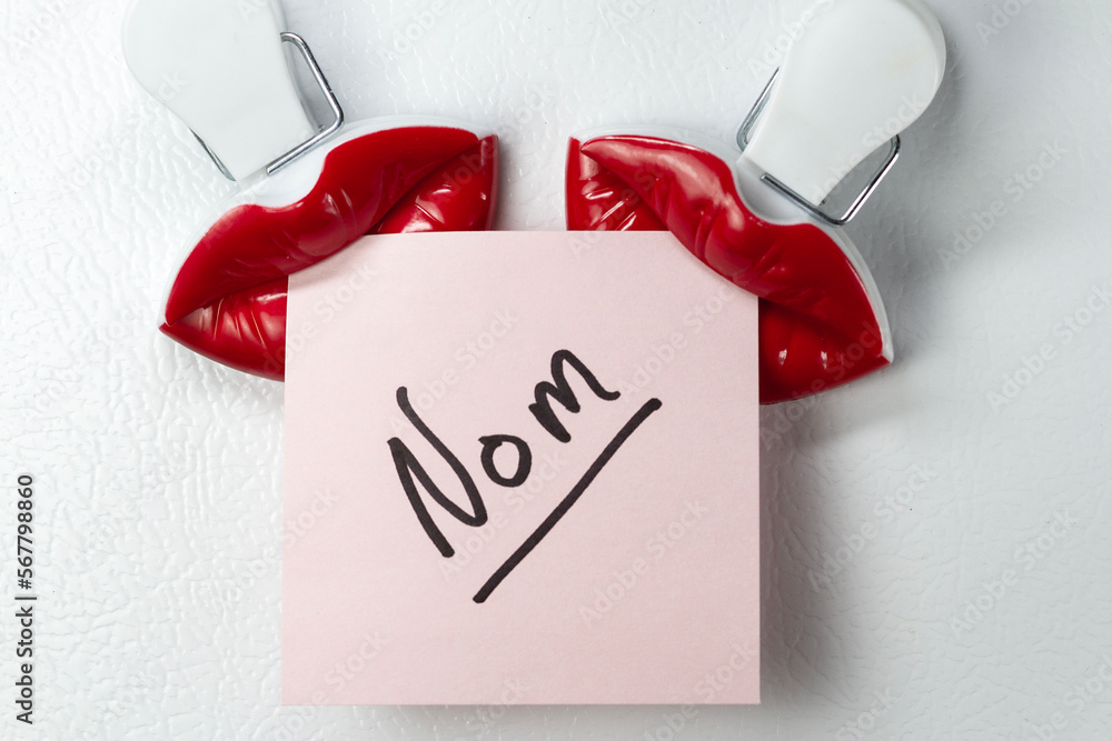 Pretty red lips holding a handwritten post note that says "nom" for ...