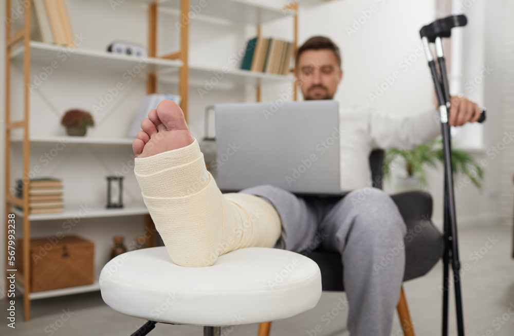 Young man with broken leg sitting in armchair with laptop. Man with ...