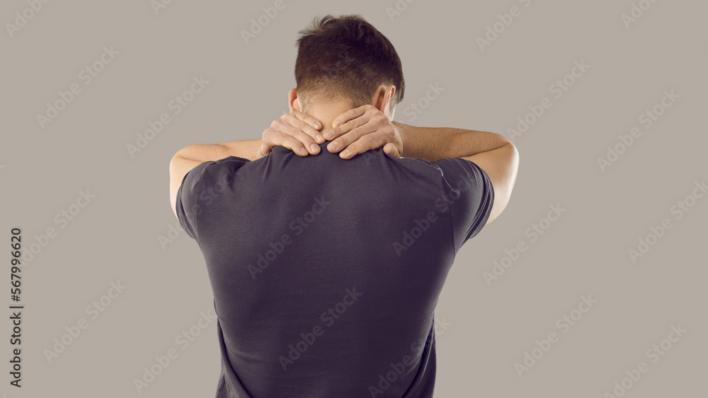 Rear view of tired young man rubbing his sore neck, isolated on gray ...