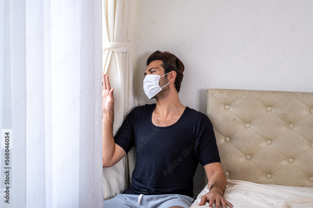 Man wearing protective mask feeling sad sitting on bed at home. Make ...