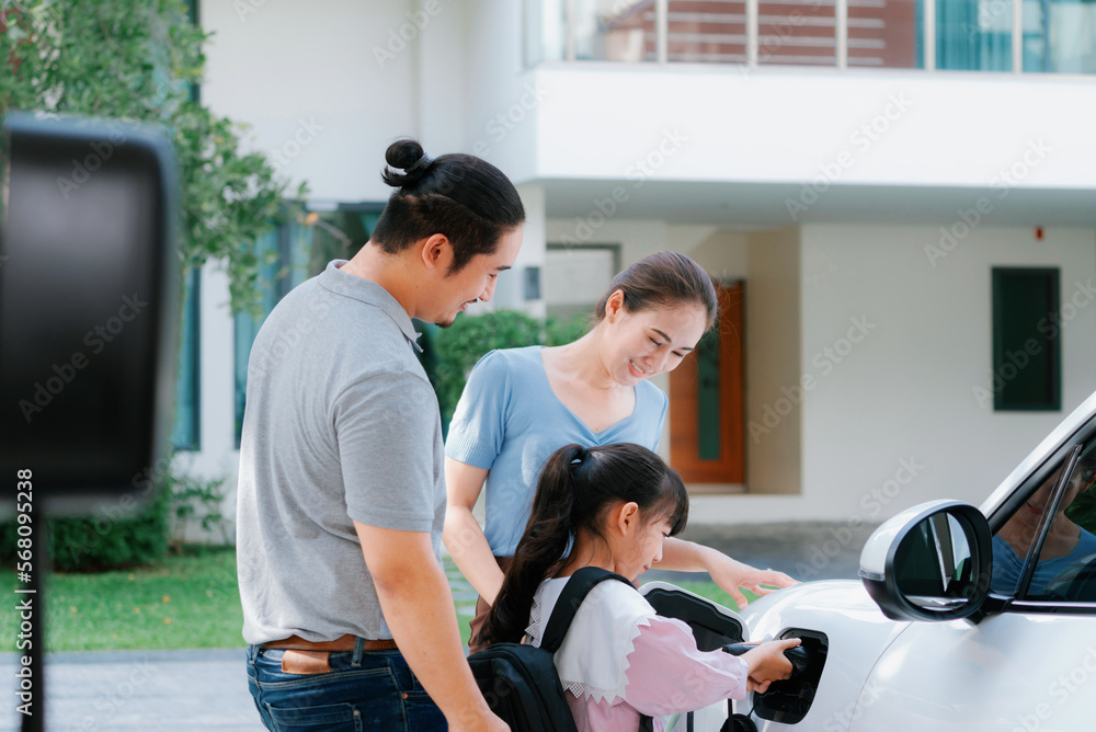 Progressive young parents and daughter with electric vehicle and home ...