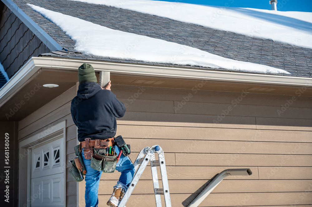 Contractor installing gutters on a residential building in the winter ...