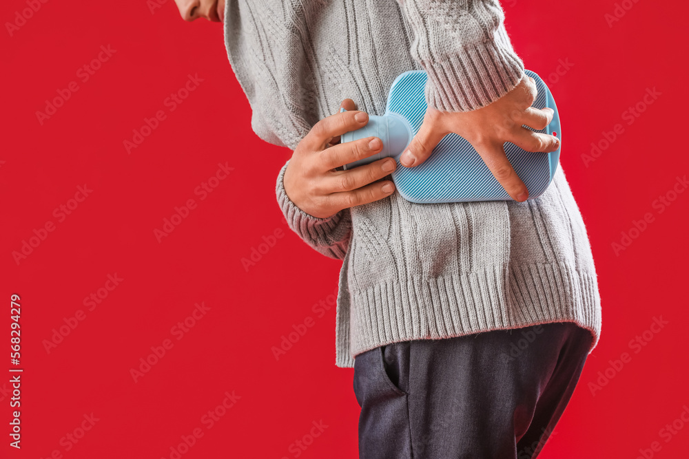 Young man warming his lower back with hot water bottle on red ...