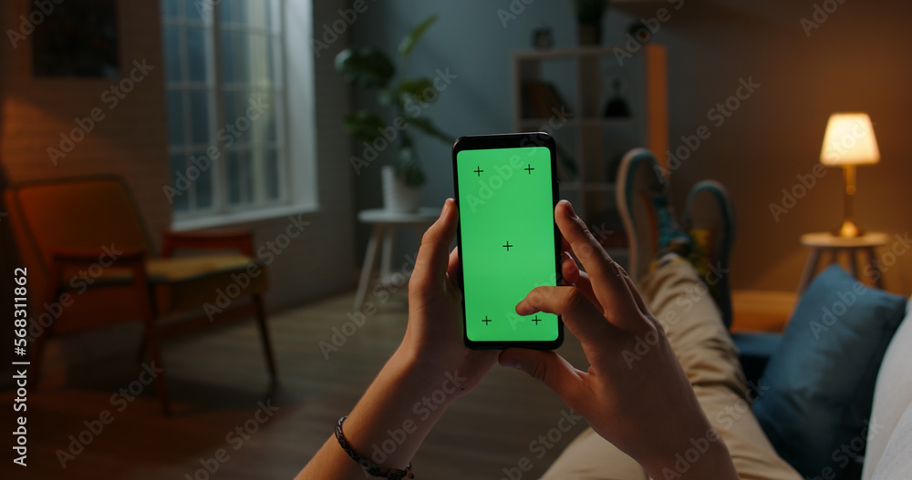 Man lying on couch using smartphone with chroma key green screen at night, scrdoing various ...